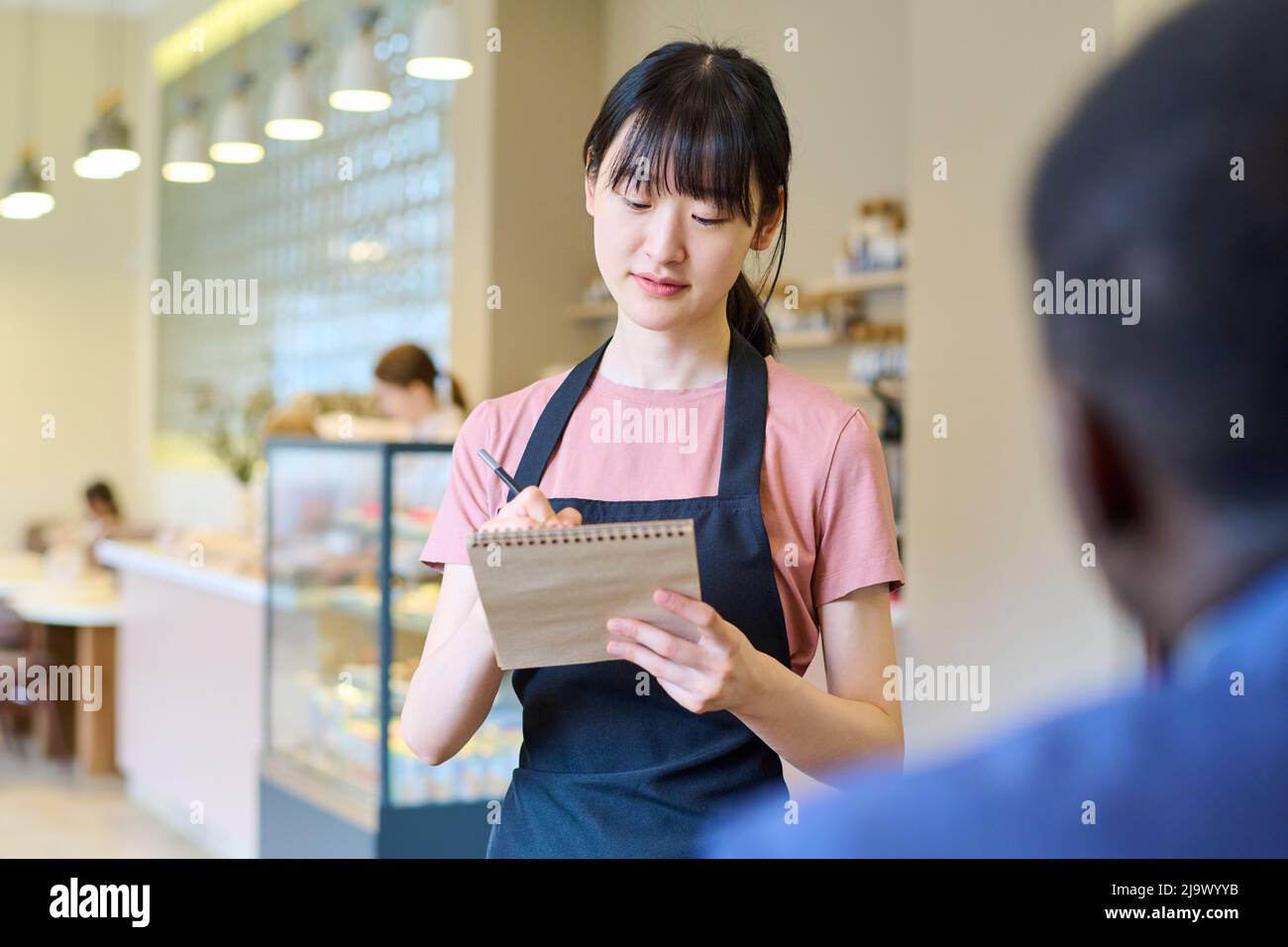 Young Asian waitress in apron making notes in notepad while taking ...