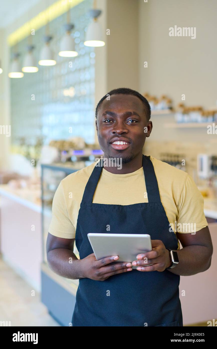 Portrait of African smiling cafe owner in apron using digital tablet at ...