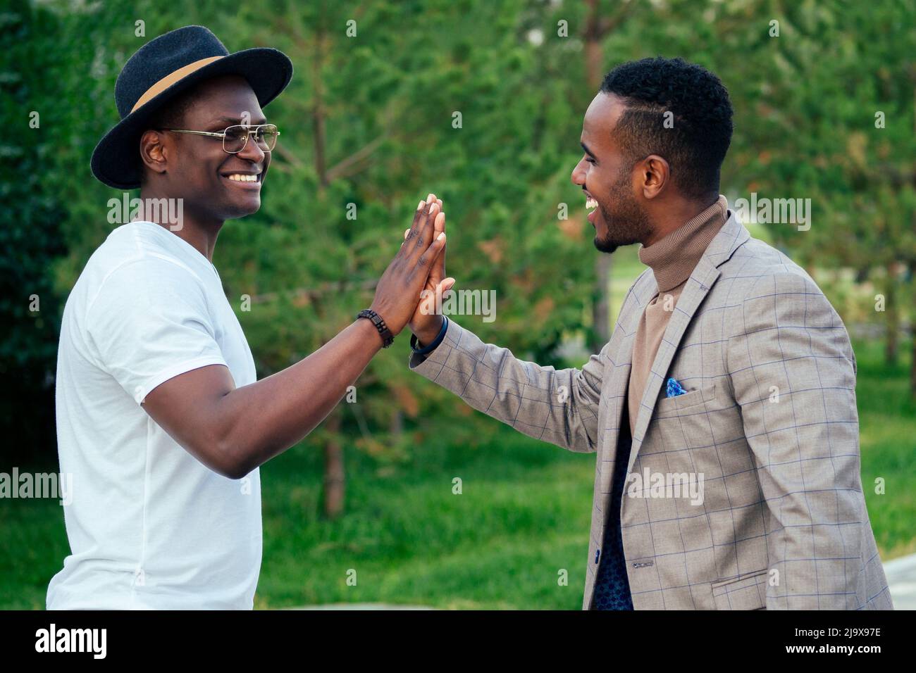 two black men in stylish suits meeting in a summer park. African ...