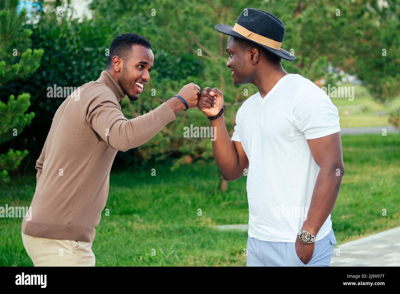 two black men in stylish suits meeting in a summer park. African ...