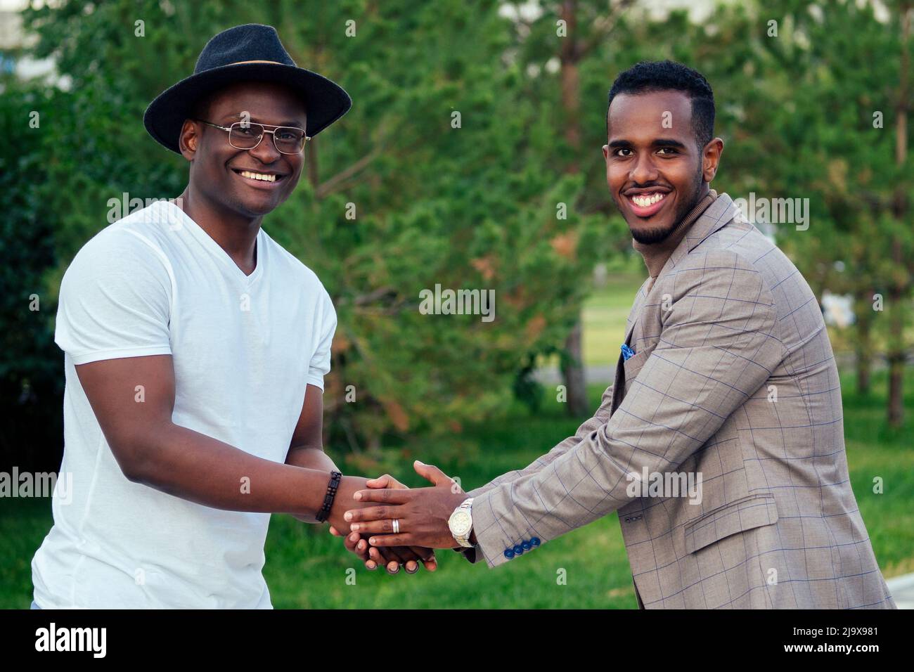 two black men in stylish suits meeting in a summer park. African ...