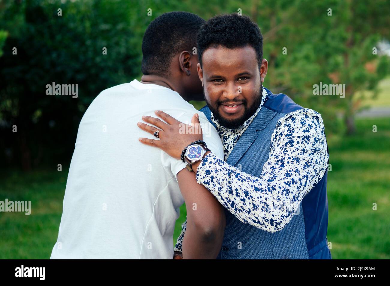 two black men in stylish suits meeting in a summer park. African ...