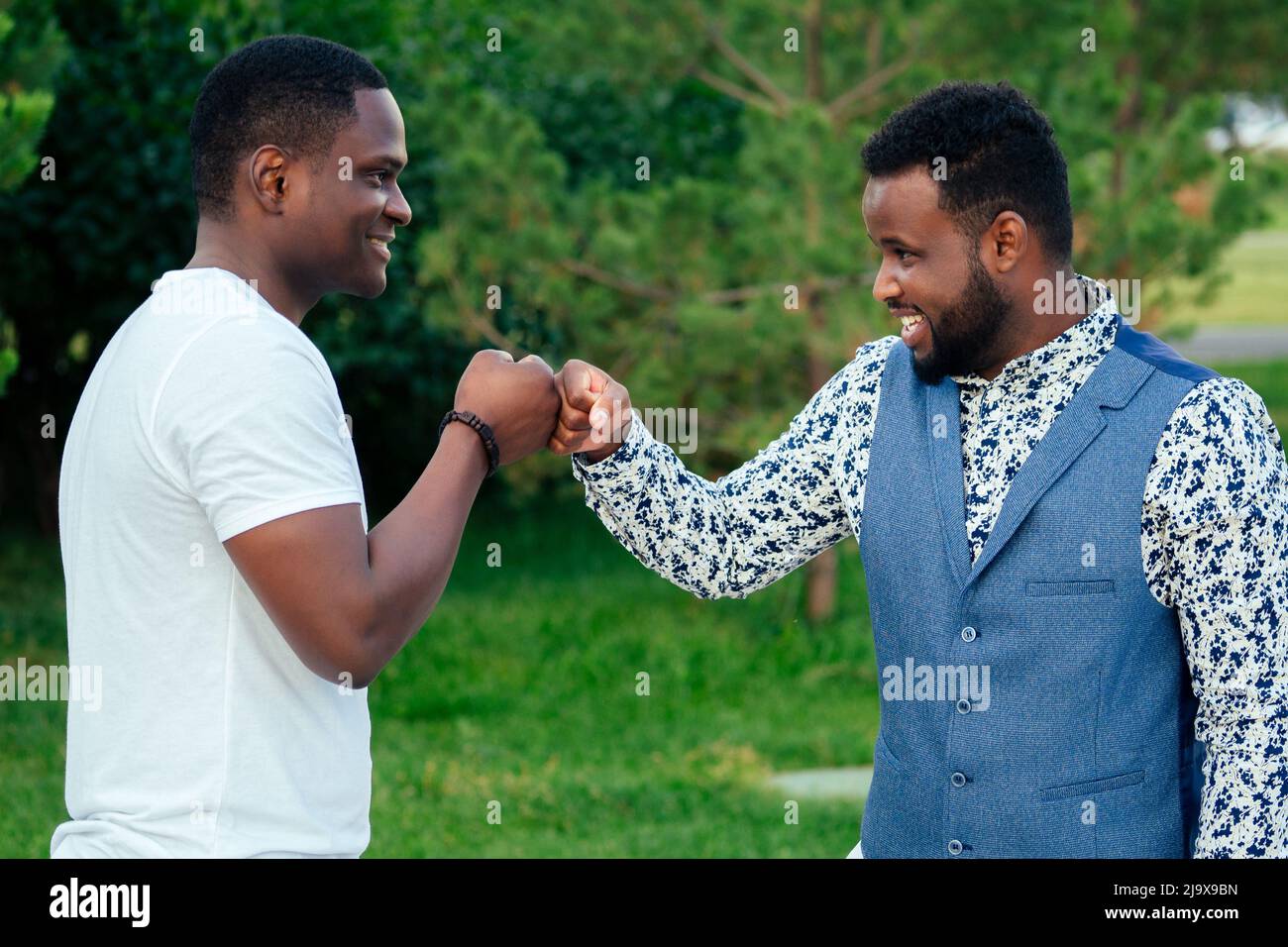 two black men in stylish suits meeting in a summer park. African ...