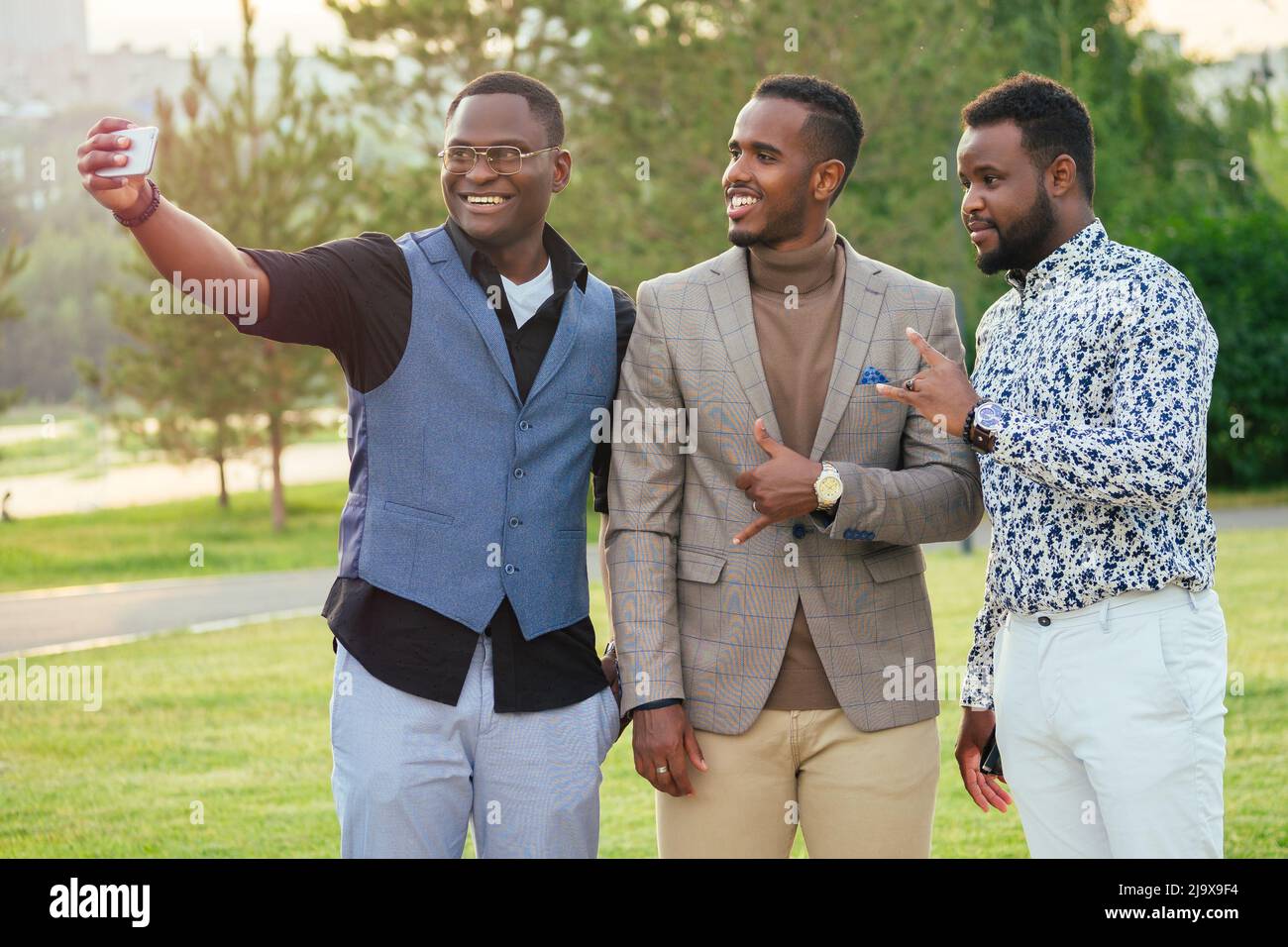 a group of three black men in stylish suits in a summer park. African ...