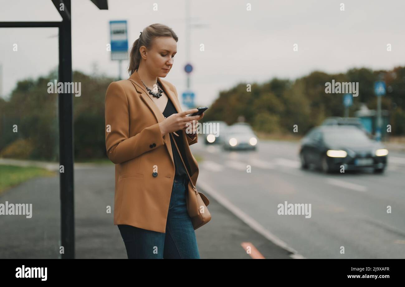 Woman with smartphone is waiting for bus at bus stop Stock Photo - Alamy