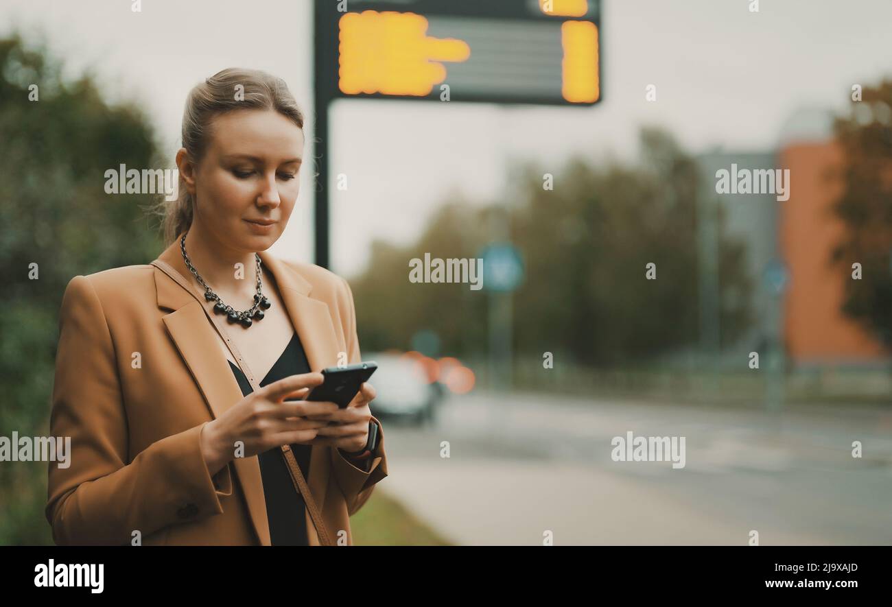 Woman with smartphone is waiting for bus at bus stop Stock Photo - Alamy