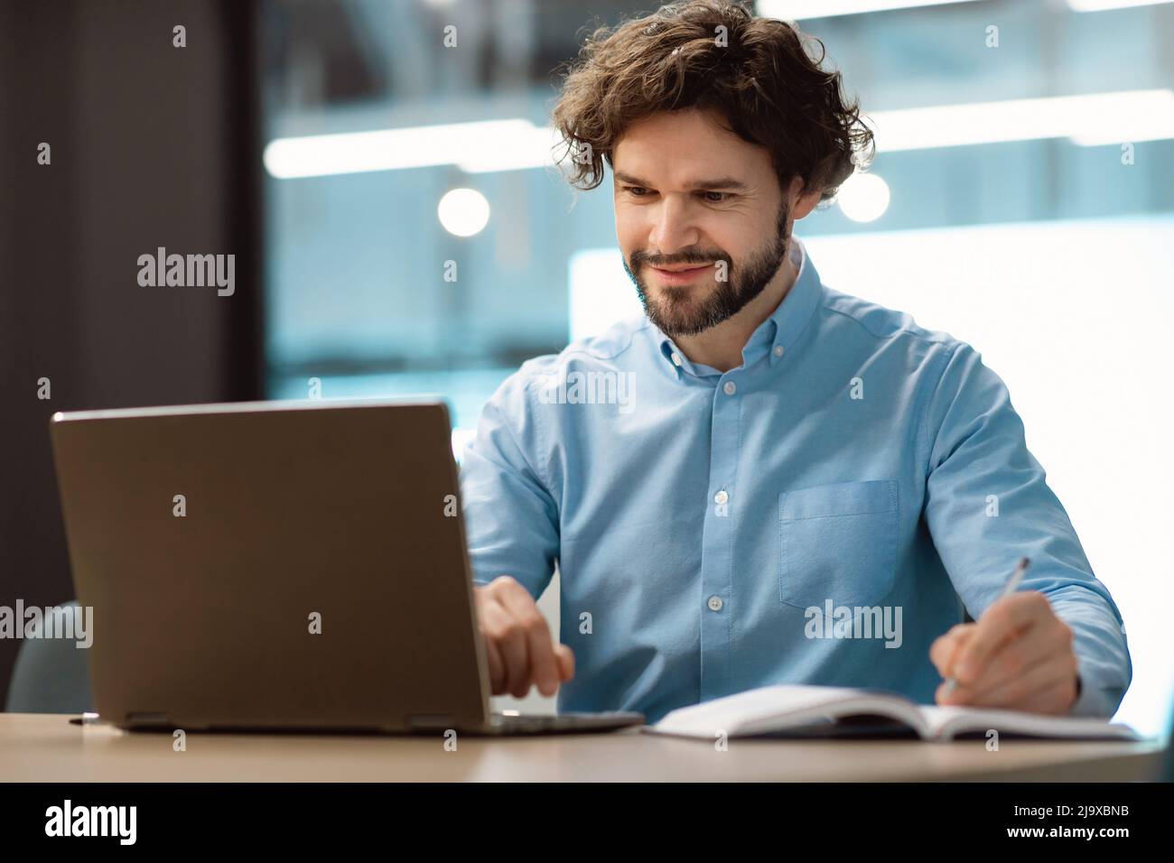 Portrait of smiling man using laptop and writing in notebook Stock ...