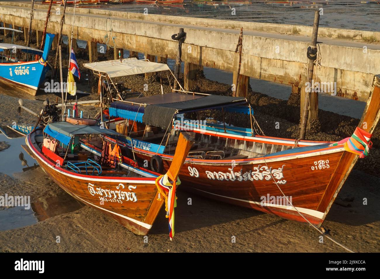 Colorful Thai fishing boats sitting on the bottom of the sea during low ...