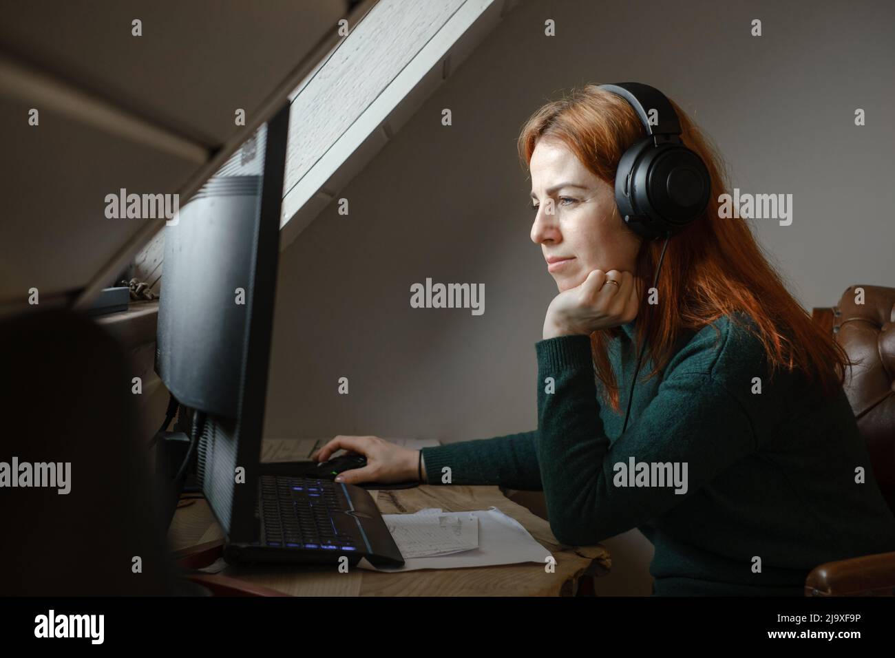Middle age woman listening to music in big headphones near computer at ...
