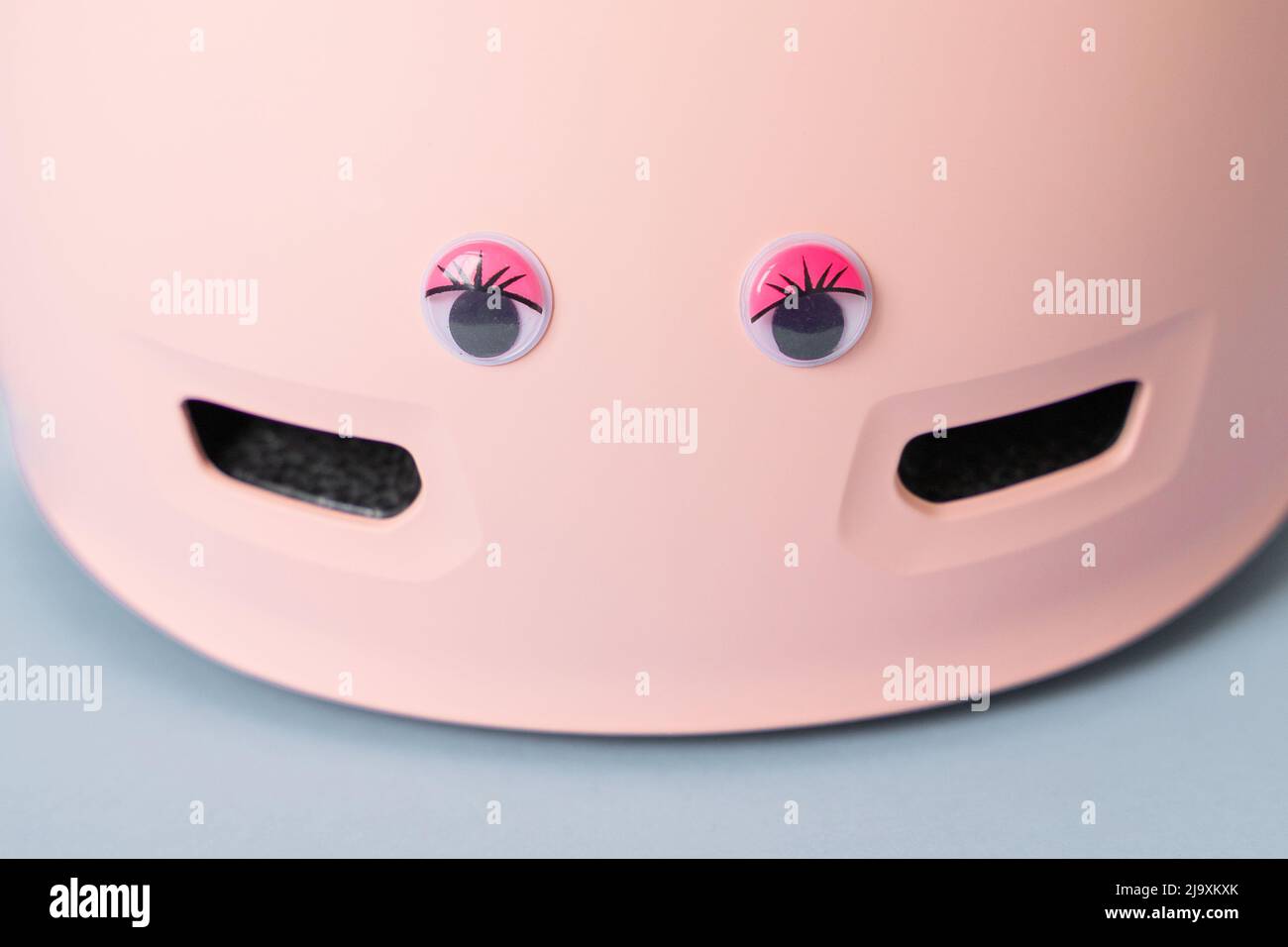 Pink helmet with funny doll eyes on blue background. Childs outdoors ...