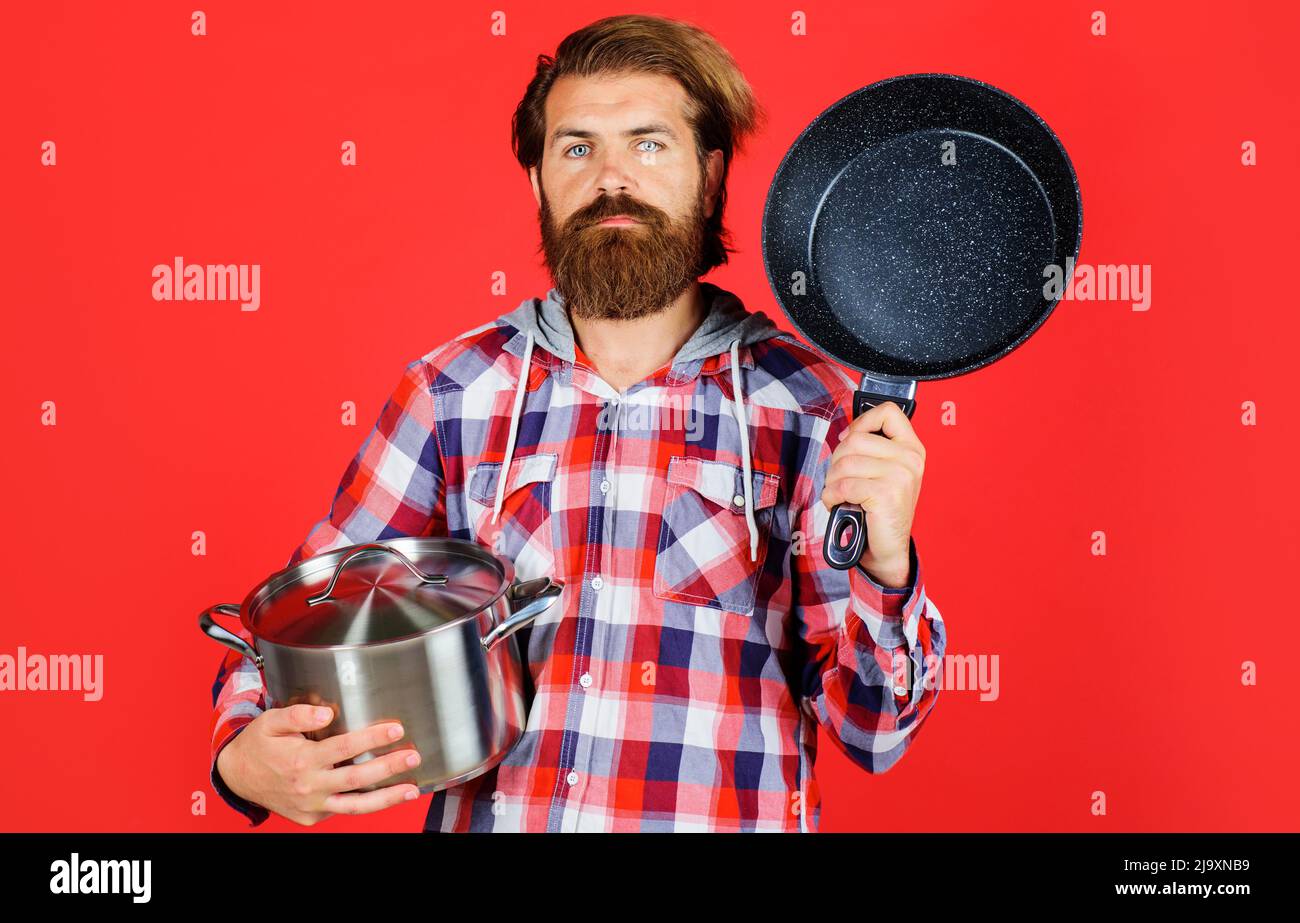 Serious bearded man with frying pan and saucepan. Cooking utensils. Guy ...