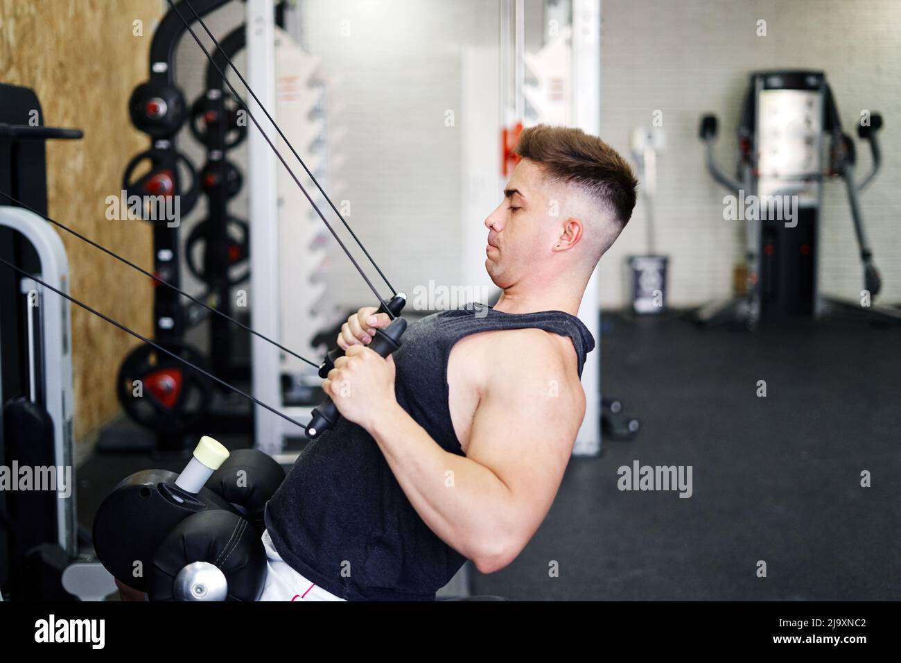 Young man sitting on exercise machines and pulling rope Stock Photo - Alamy