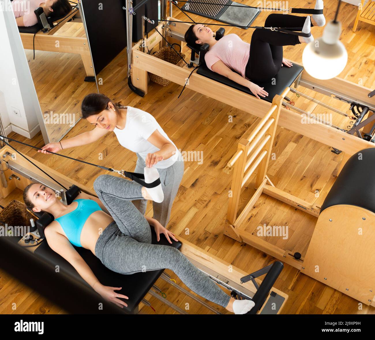 View from above of trainer helping young woman practicing Pilates on ...