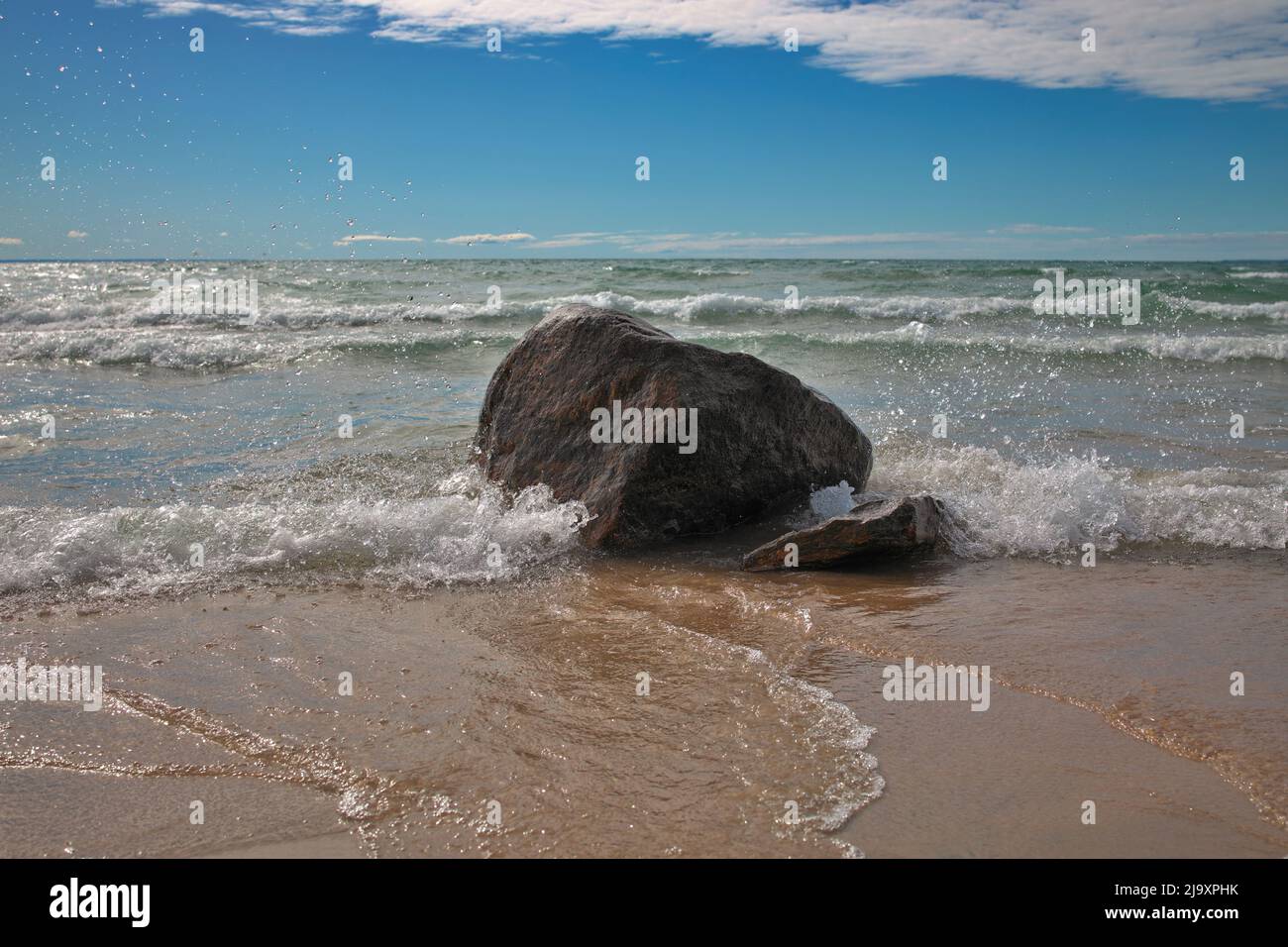 Waves Crash into a Backlit Boulder at a Beautiful Sandy Beach with Blue ...