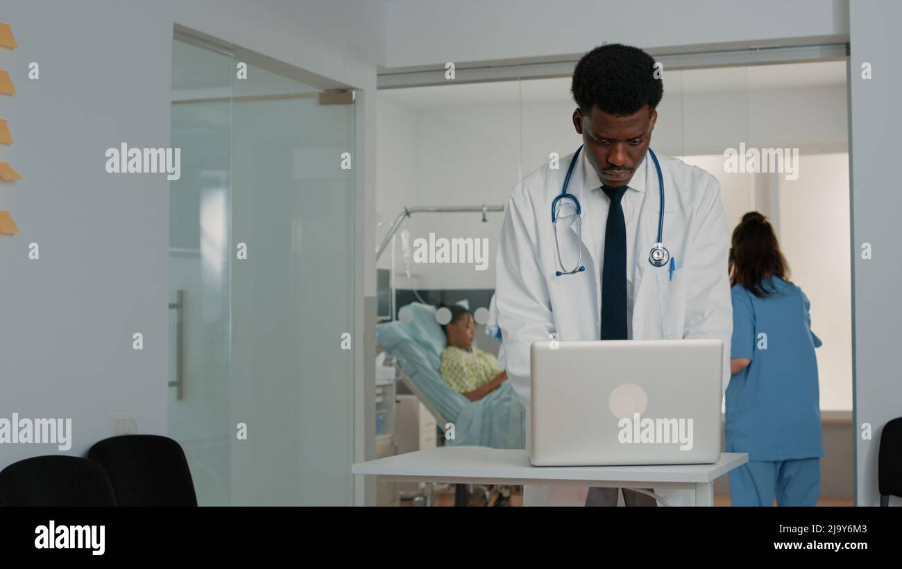 Doctor using laptop to treat patient in hospital ward while nurse ...