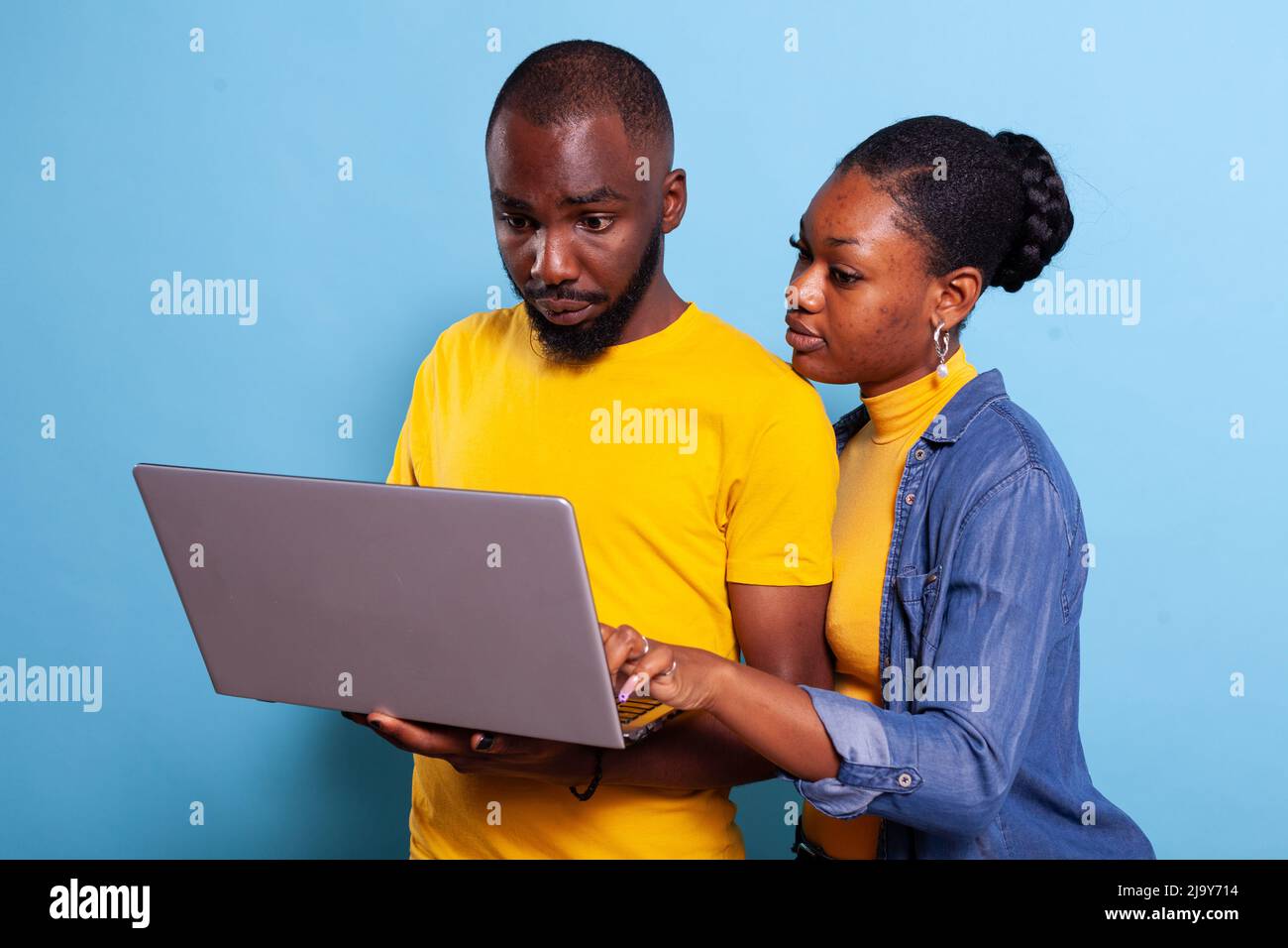 Modern couple looking at laptop screen over blue background, browsing ...
