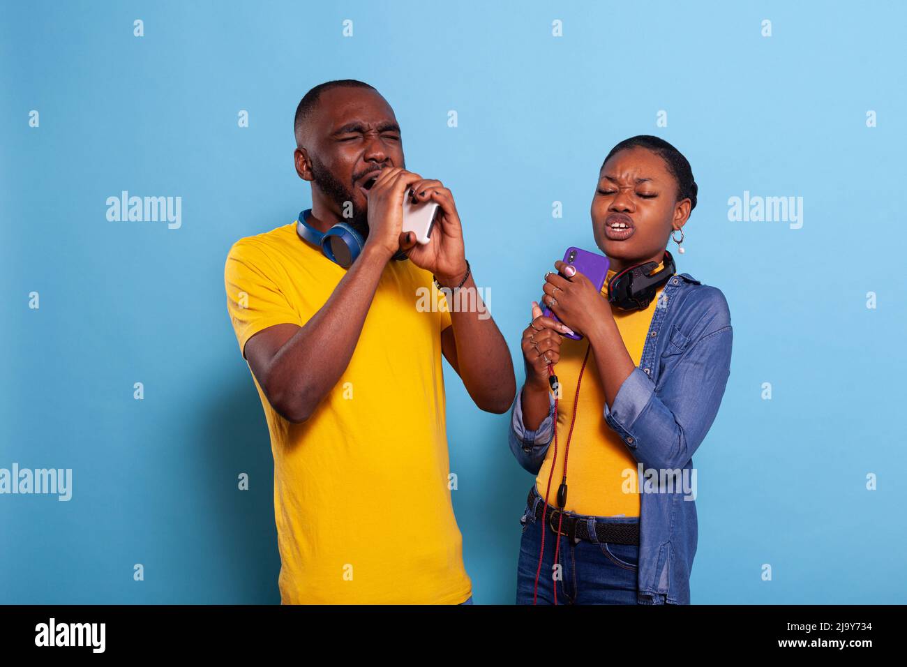 Happy couple using smartphone as microphone to sing song, wearing ...