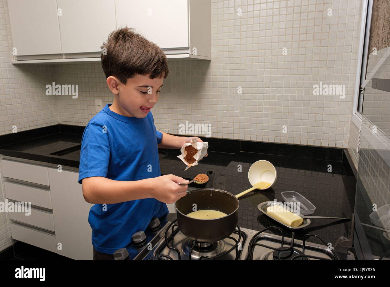8 year old child putting a spoon of cocoa powder in condensed milk to ...