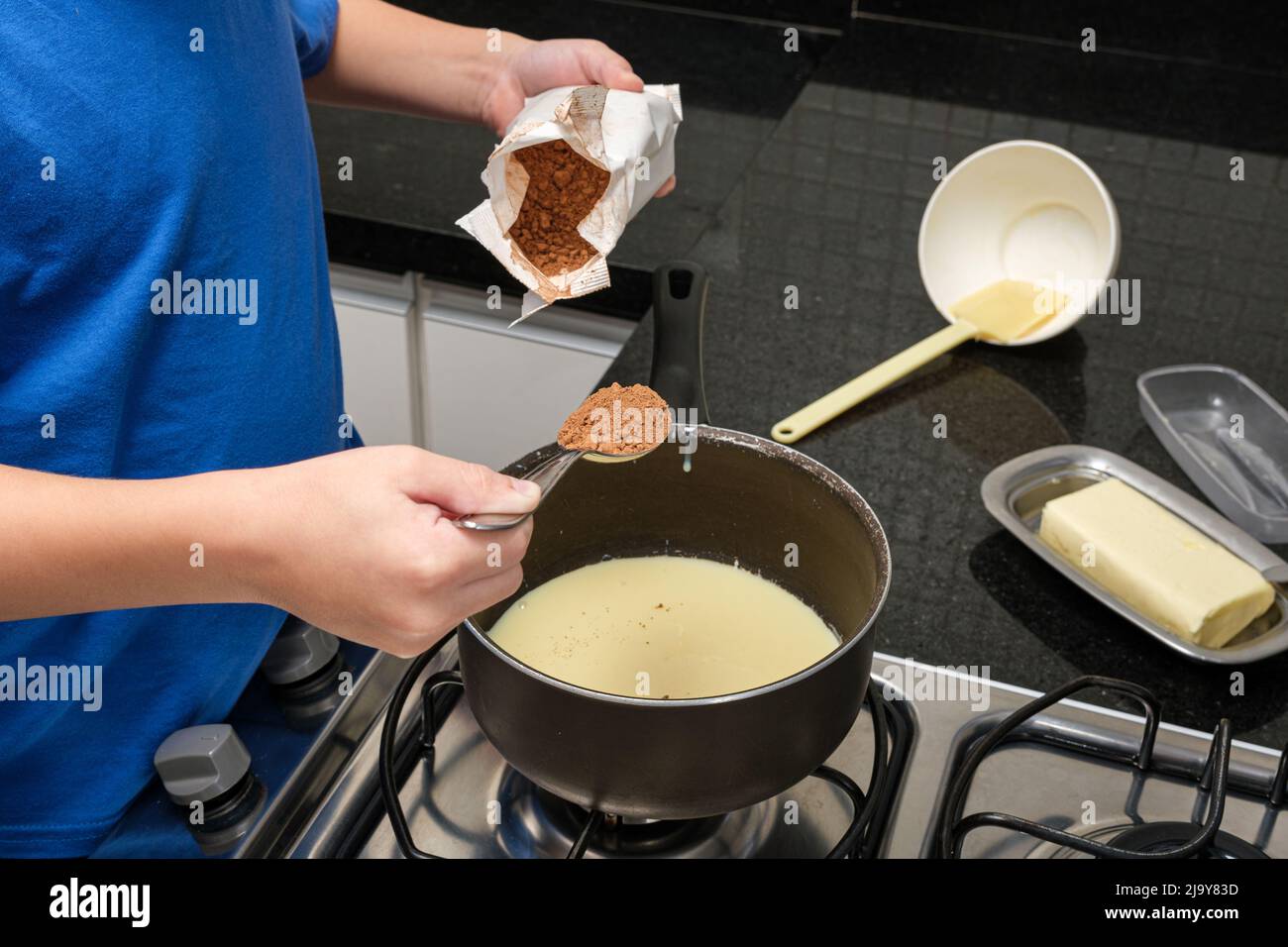 Closeup of a child's hand pouring a spoonful of cocoa powder into ...