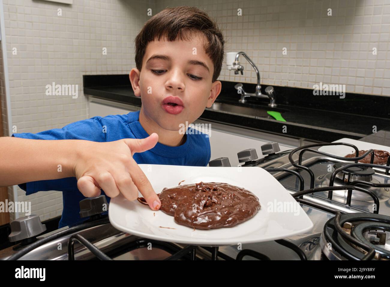 8 year old child putting his finger on the plate with sweet brigadeiro ...