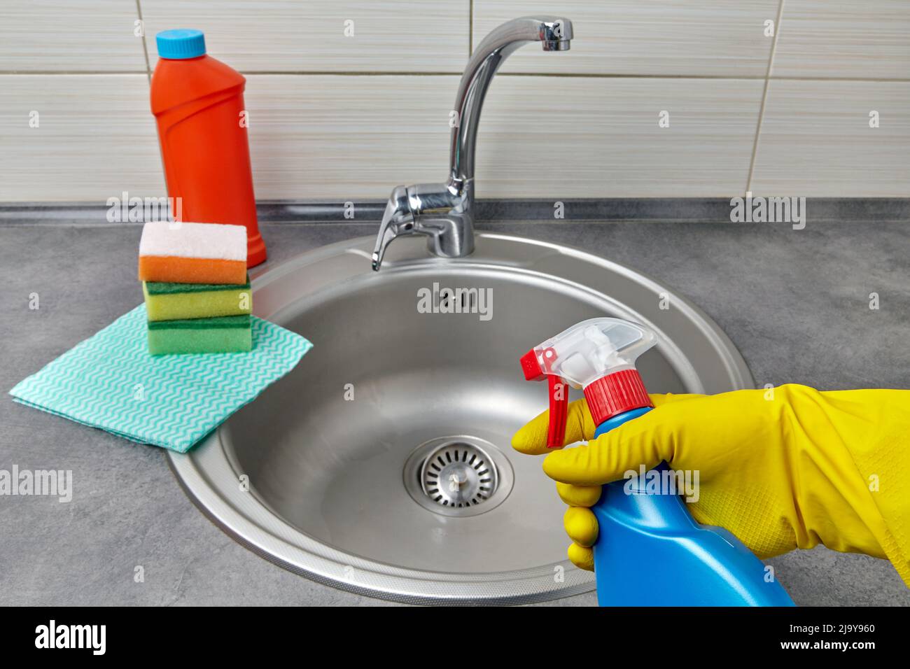 Hands in yellow rubber gloves hold a spray bottle with cleaning agent ...