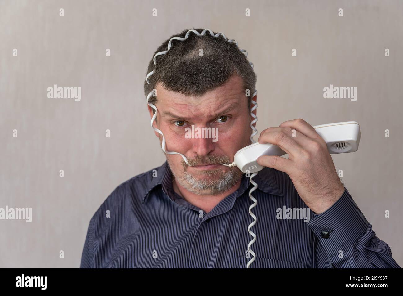 Portrait of a grown man wrapping a telephone cord around his head. A ...