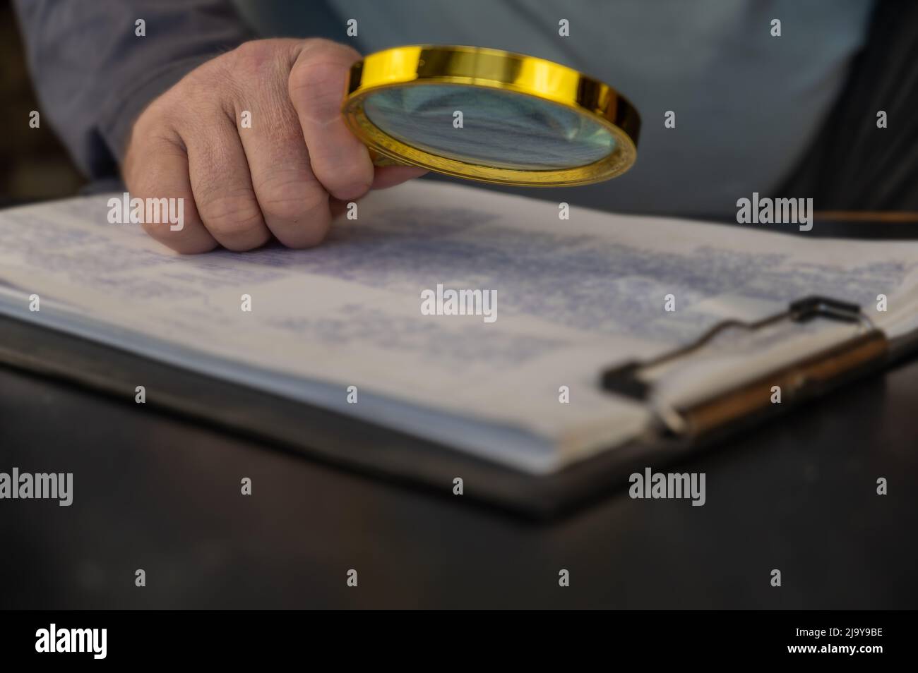 Handholds a gold-rimmed magnifying glass atop a clipboard. Adult male ...
