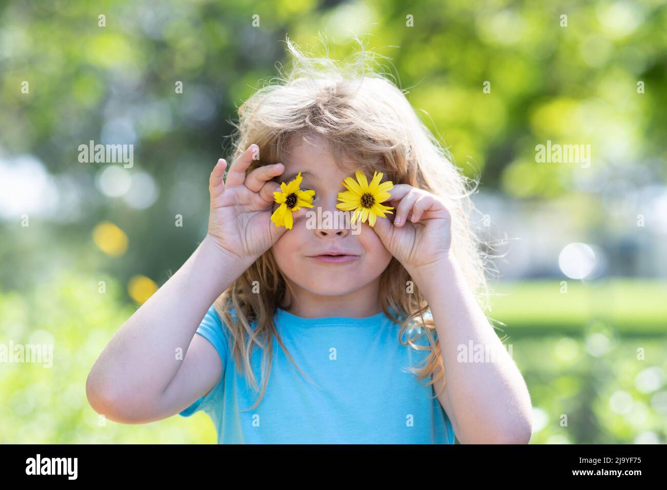 Spring kids portrait, funny face. Little child boy is smelling flowers ...