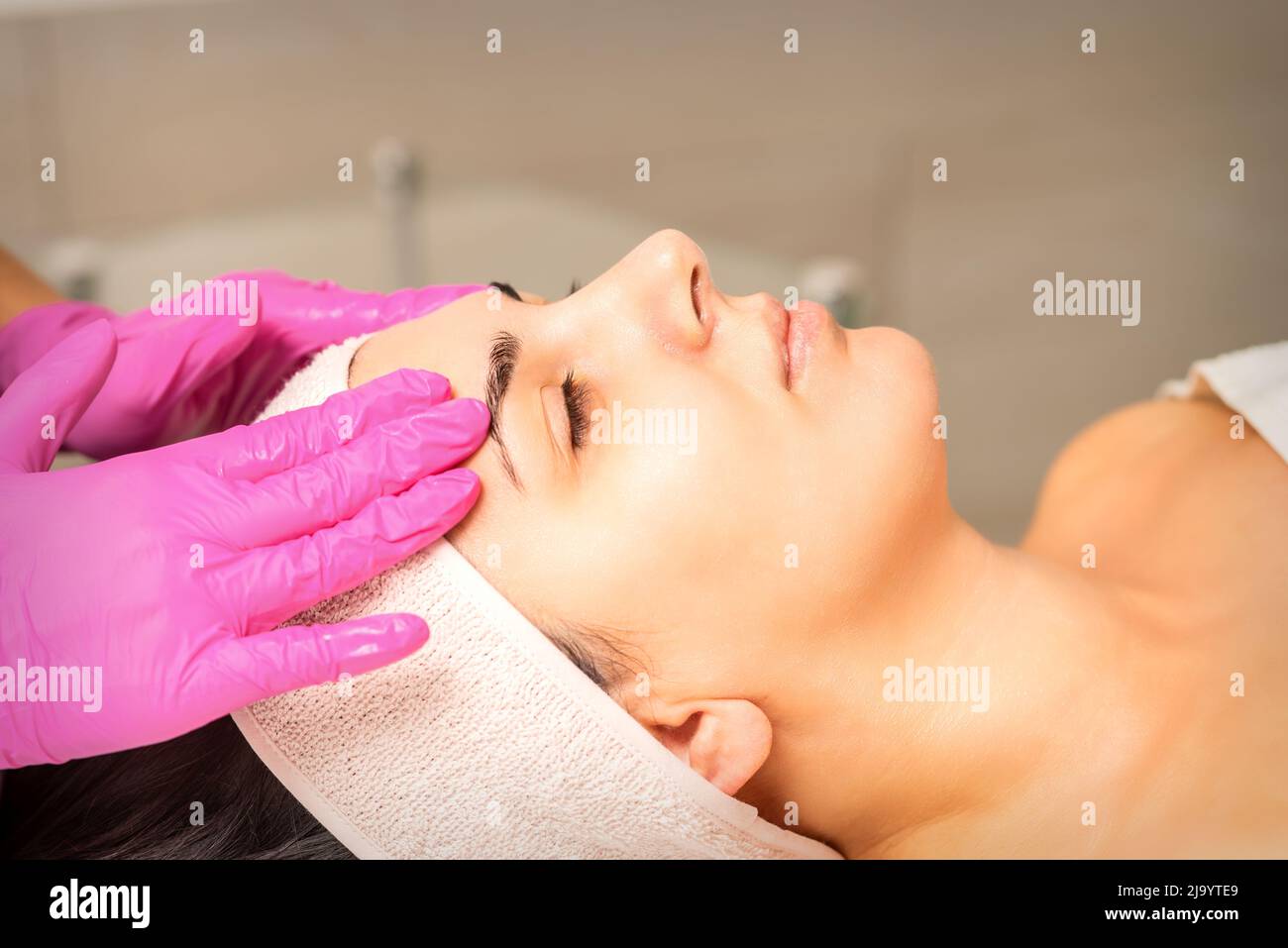 Cosmetologist with gloved hands applies a moisturizing mask with ...