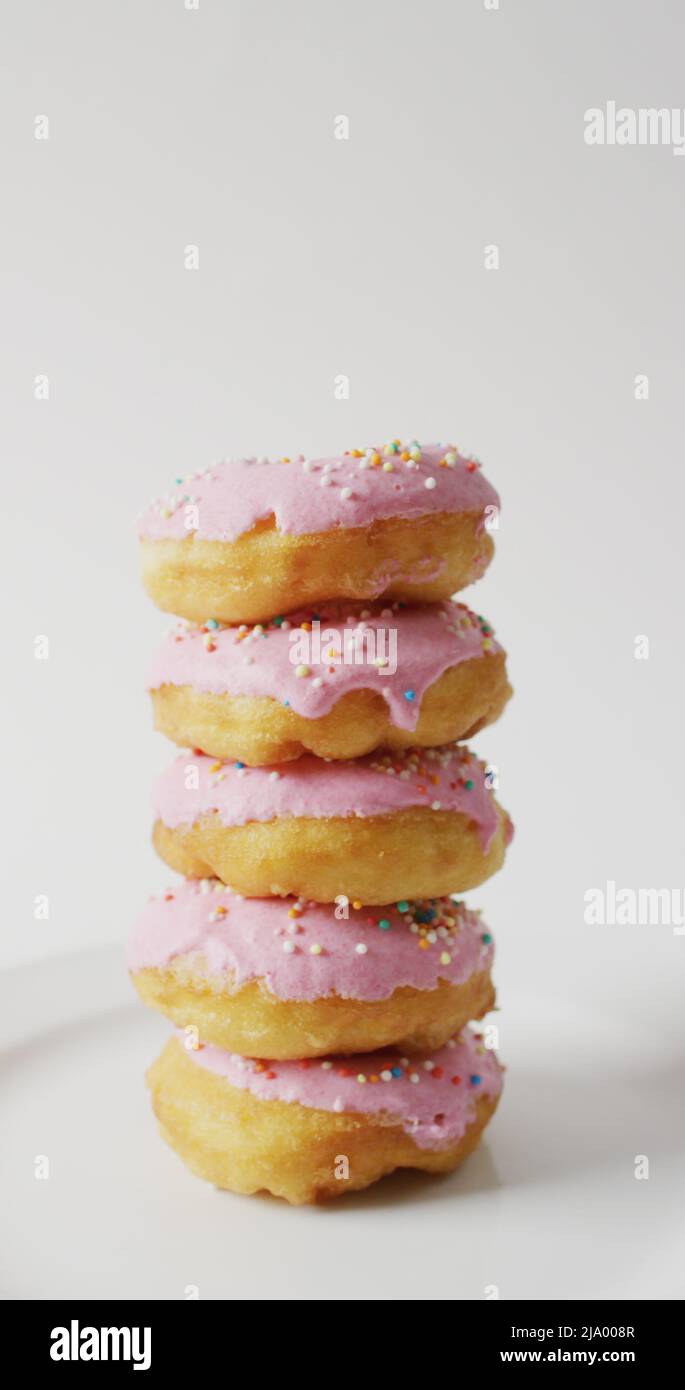 Vertical image of stack of donuts with pink frosting on grey background ...