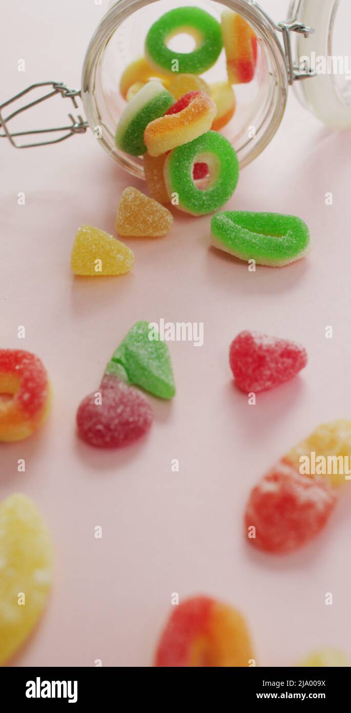 Vertical image of jelly candy spilling out of glass jar on pink ...