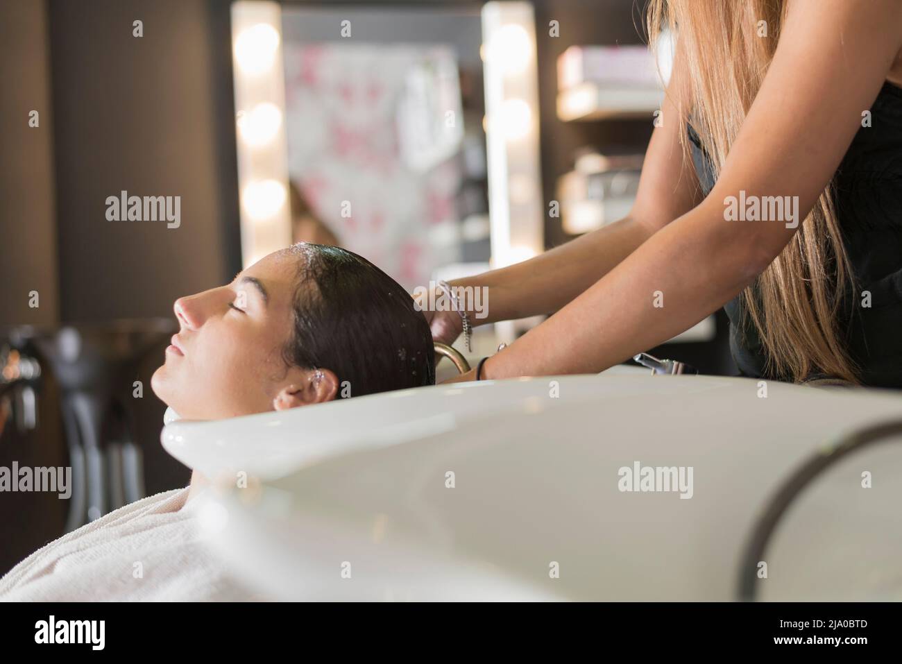 Side view of a hairdresser washing hair of a beautiful lady in hair ...