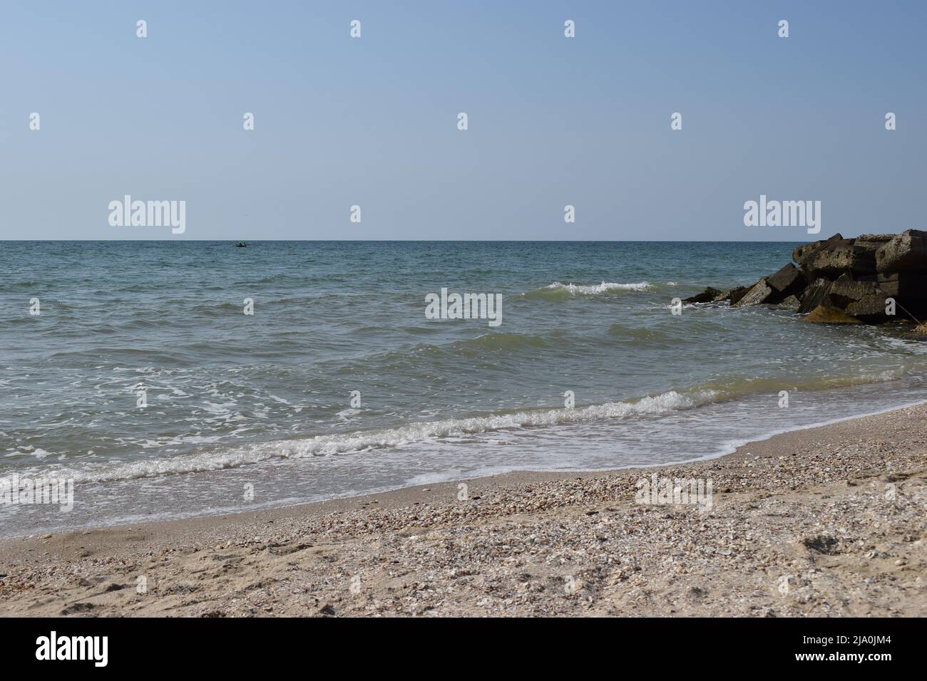 The waves of the turquoise sea break on the coastal boulders and a ...