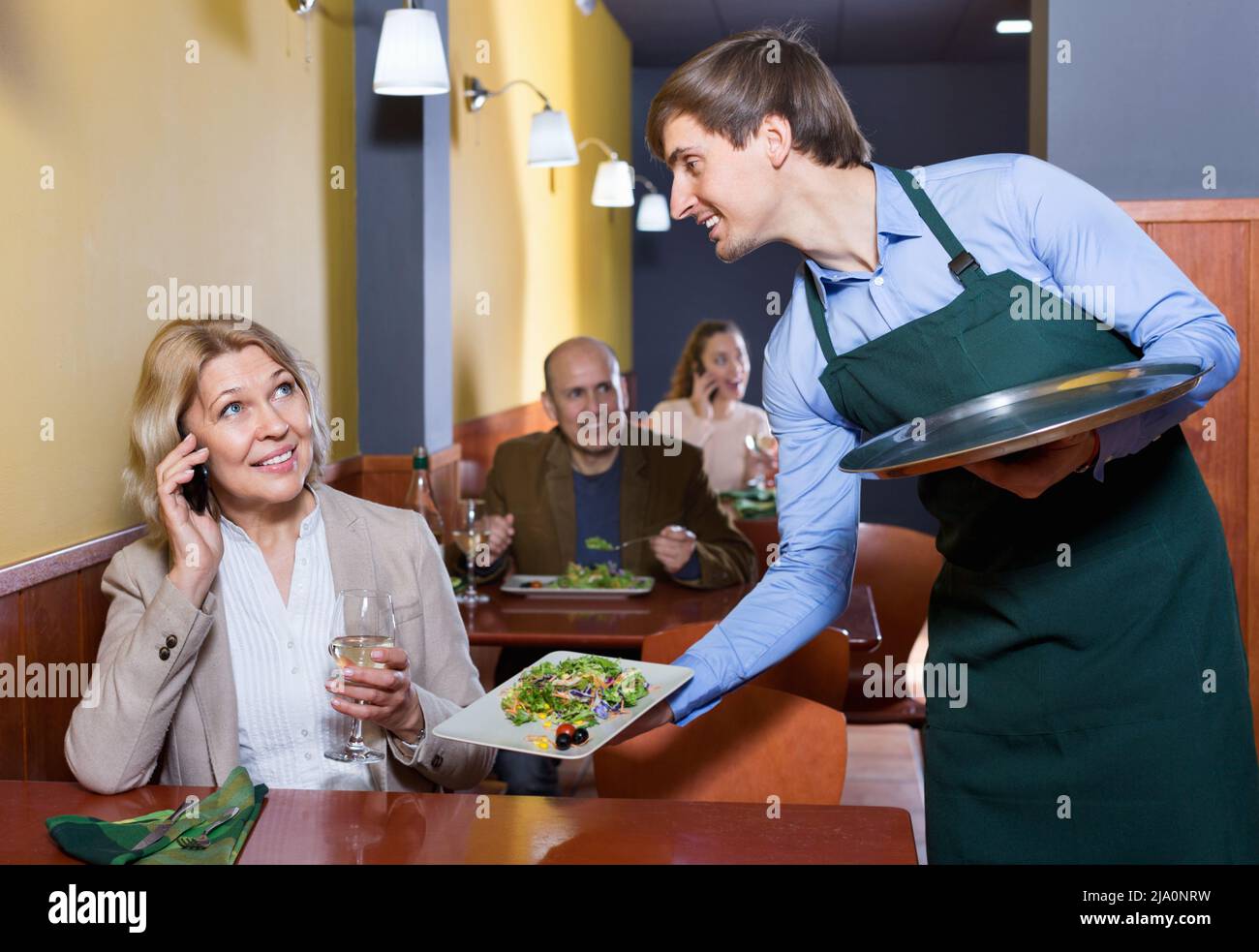 Positive waiter bringing order to charming smiling mature female Stock ...