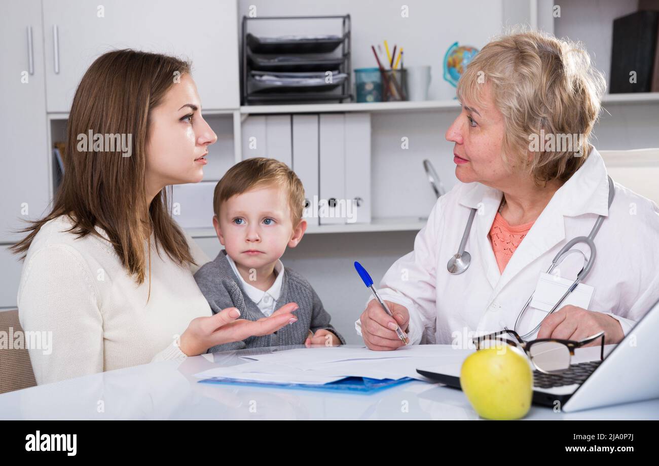 Pediatrist woman is examining kid and talking to his puzzled mother ...