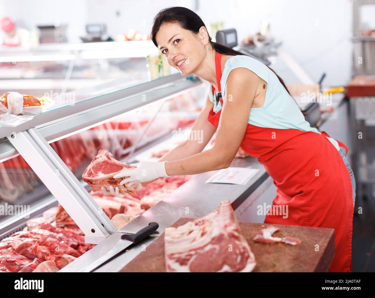 Adult woman seller displaying fresh meat in shop Stock Photo - Alamy