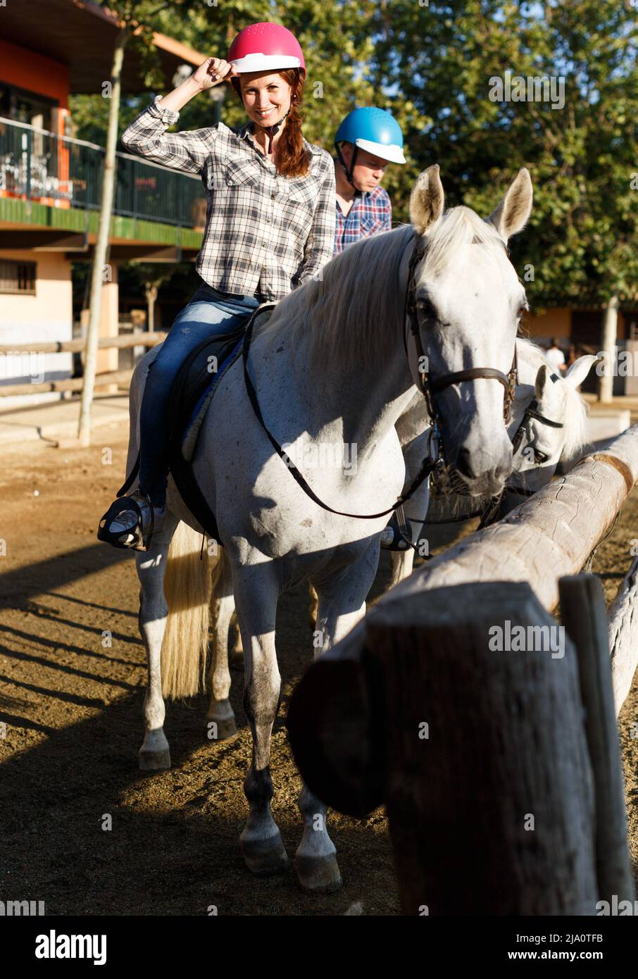 Woman and man in helmets training riding horse at farm at summer day ...