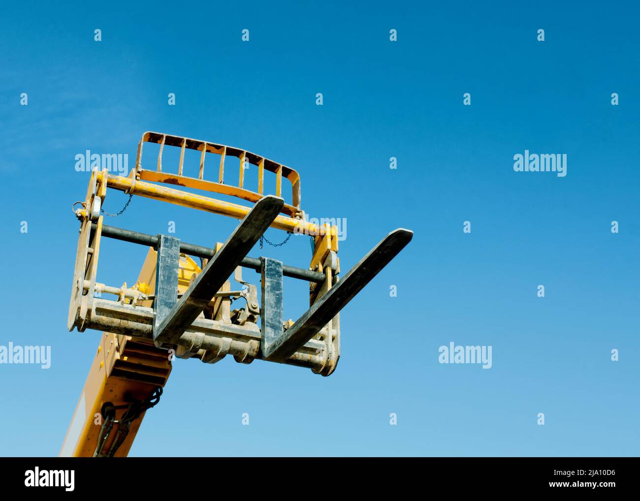 Telehandler with raised boom and forks on clear blue sky background ...