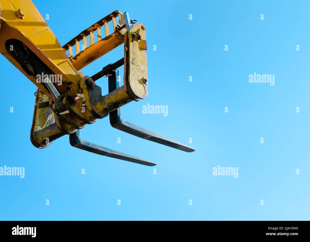 Telehandler with raised boom and forks on clear blue sky background ...