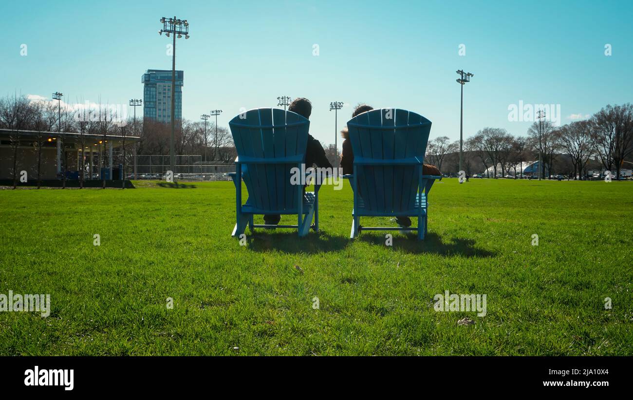 Two friends sitting on wooden chairs in the park. Back view Stock Photo ...