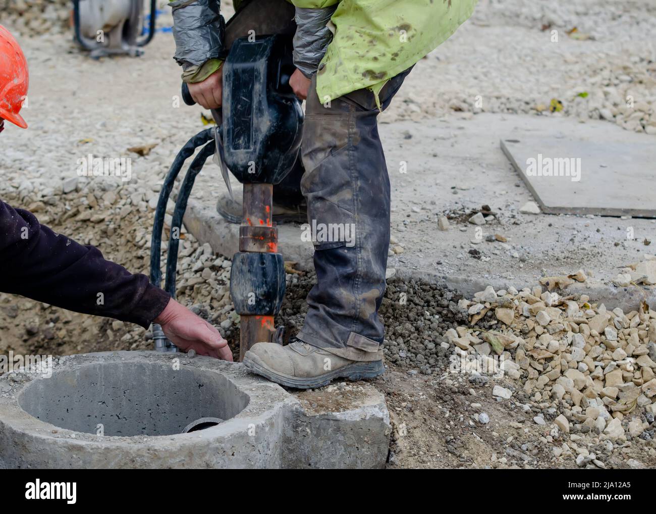 Construction worker breaking concrete around road gully using hydraulic ...