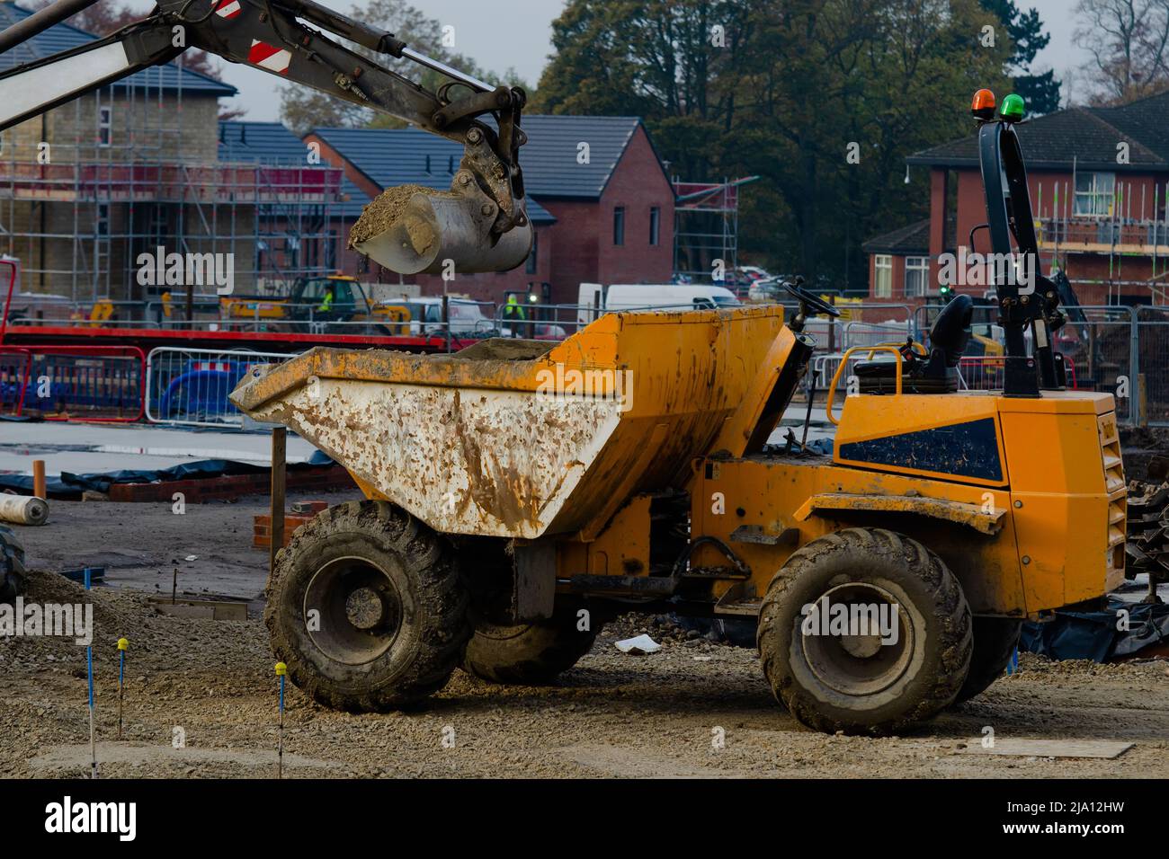 Houses under construction and excavator loading dumper with stone in ...