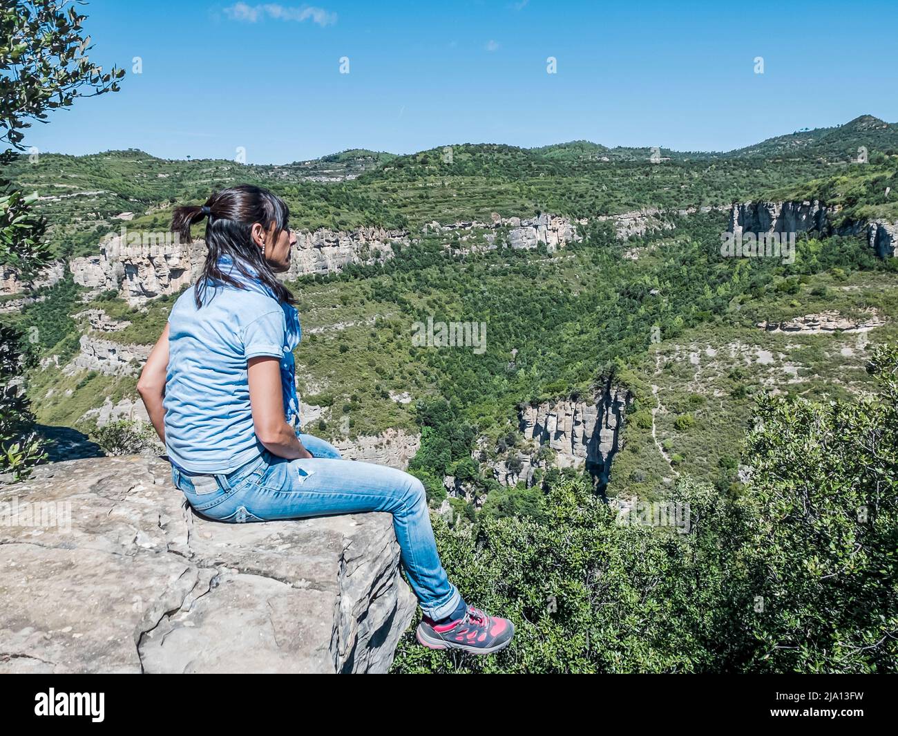 Young traveling woman sitting on the top of the mountain cliff with relaxing mood and watching ...