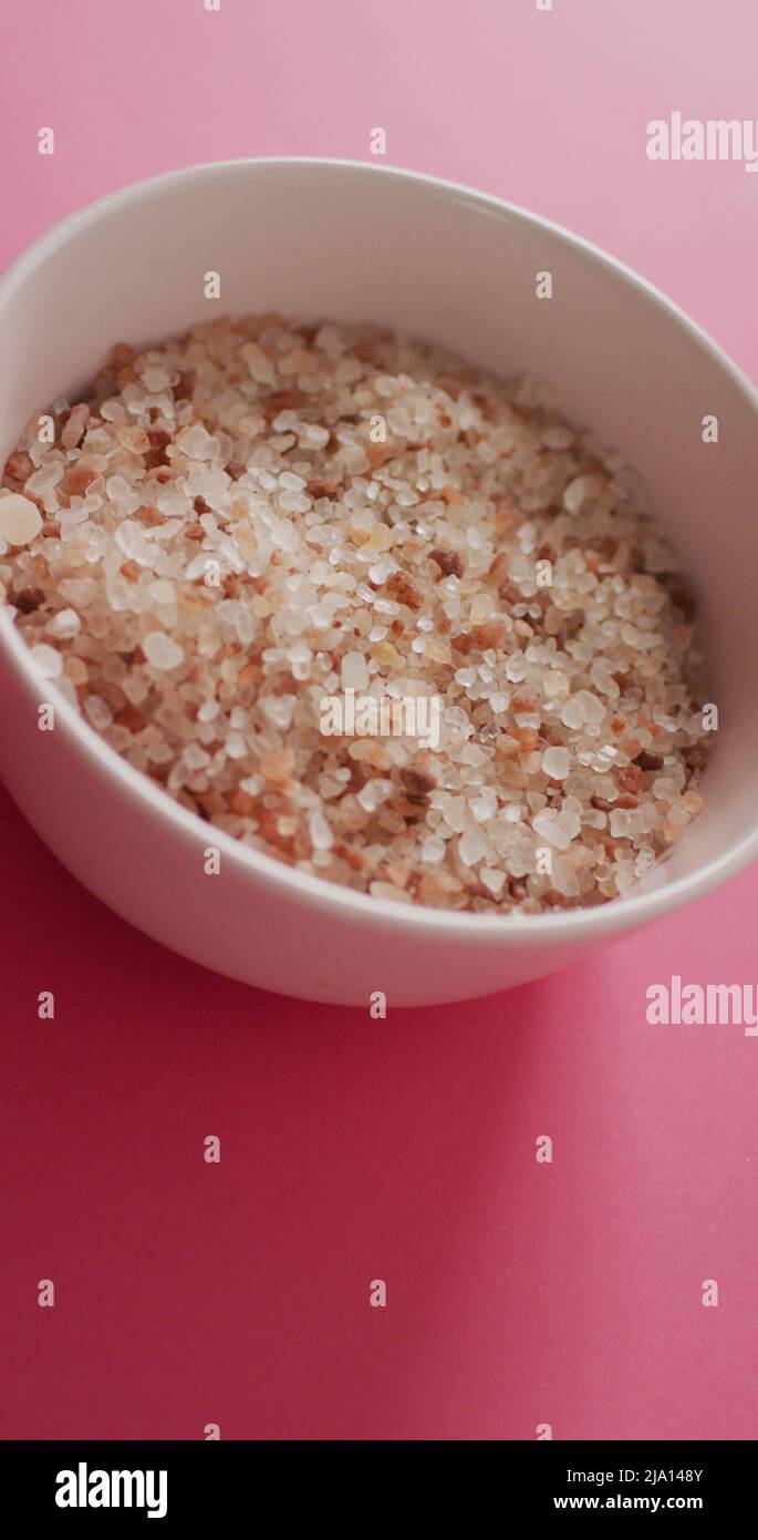 Vertical image of flavoured salt crystals falling into bowl on pink ...