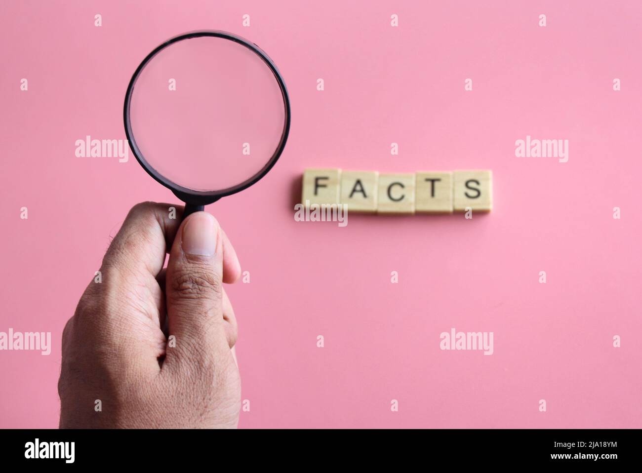 Hand holding magnifying glass and wooden cubes with text FACTS ...