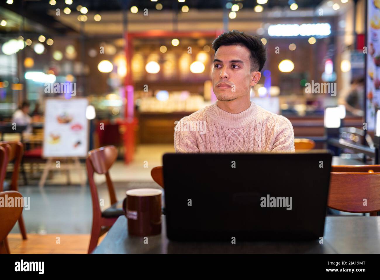 Portrait of handsome young man using laptop computer at coffee shop ...