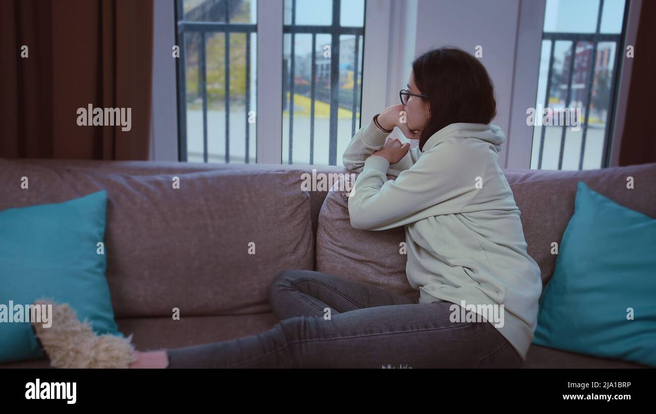 Girl thinking, looking out the window while sitting on the couch, copy ...