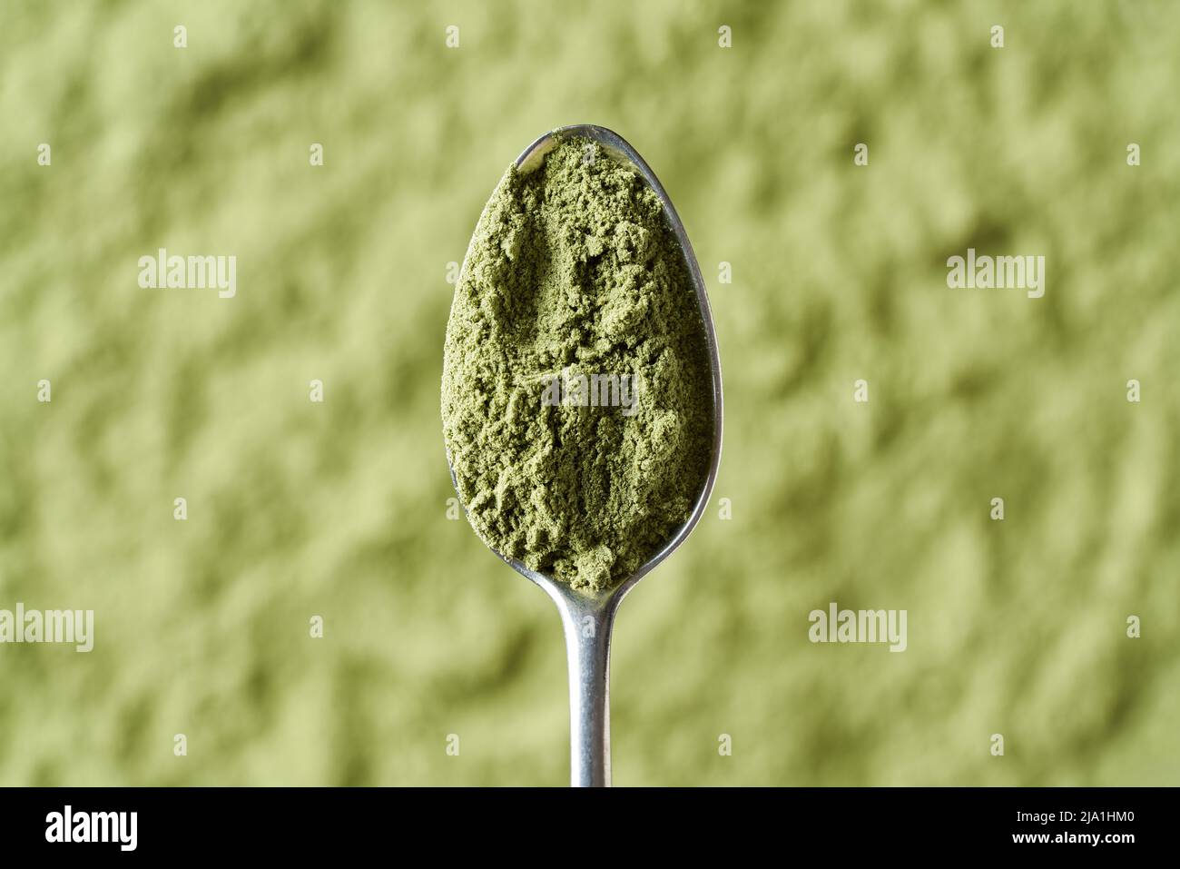 Dry barley grass powder on a spoon over green background - healthy ...