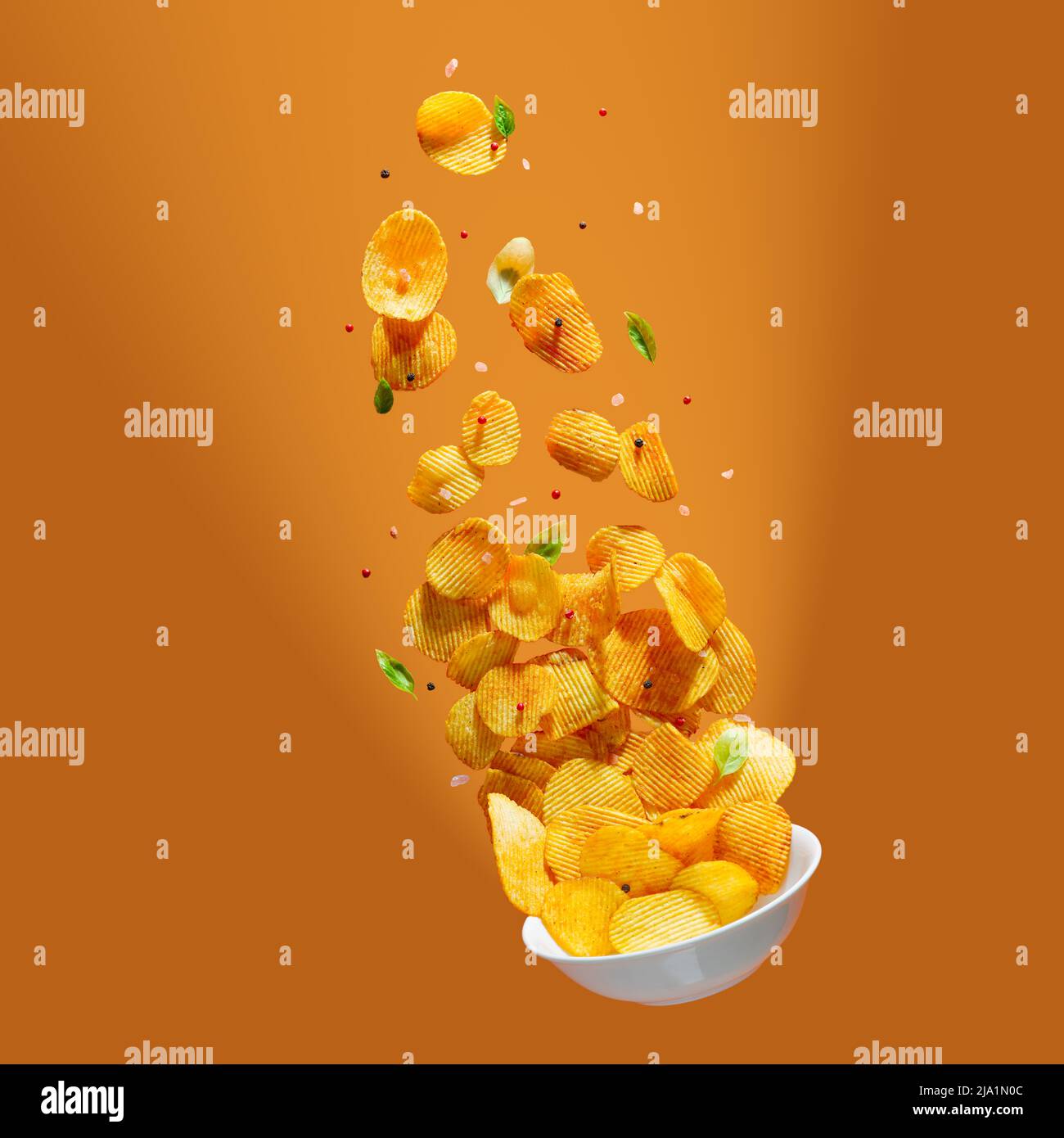 Potato chips falling onto plate on white background. Advertising ...