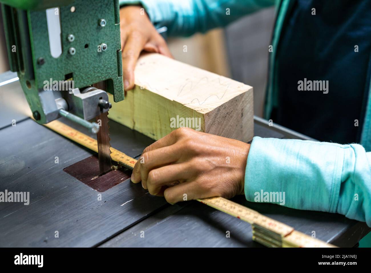 A close-up of a woman carpenter cutting a block of wood with a band saw ...